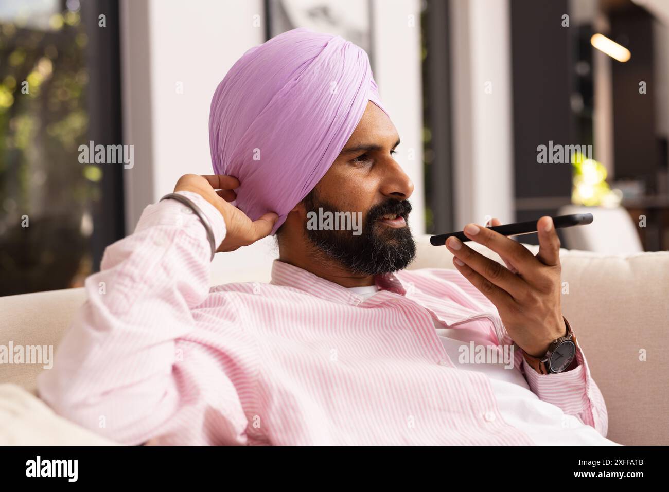 Speaking into smartphone, Indian man relaxing on couch at home Stock ...