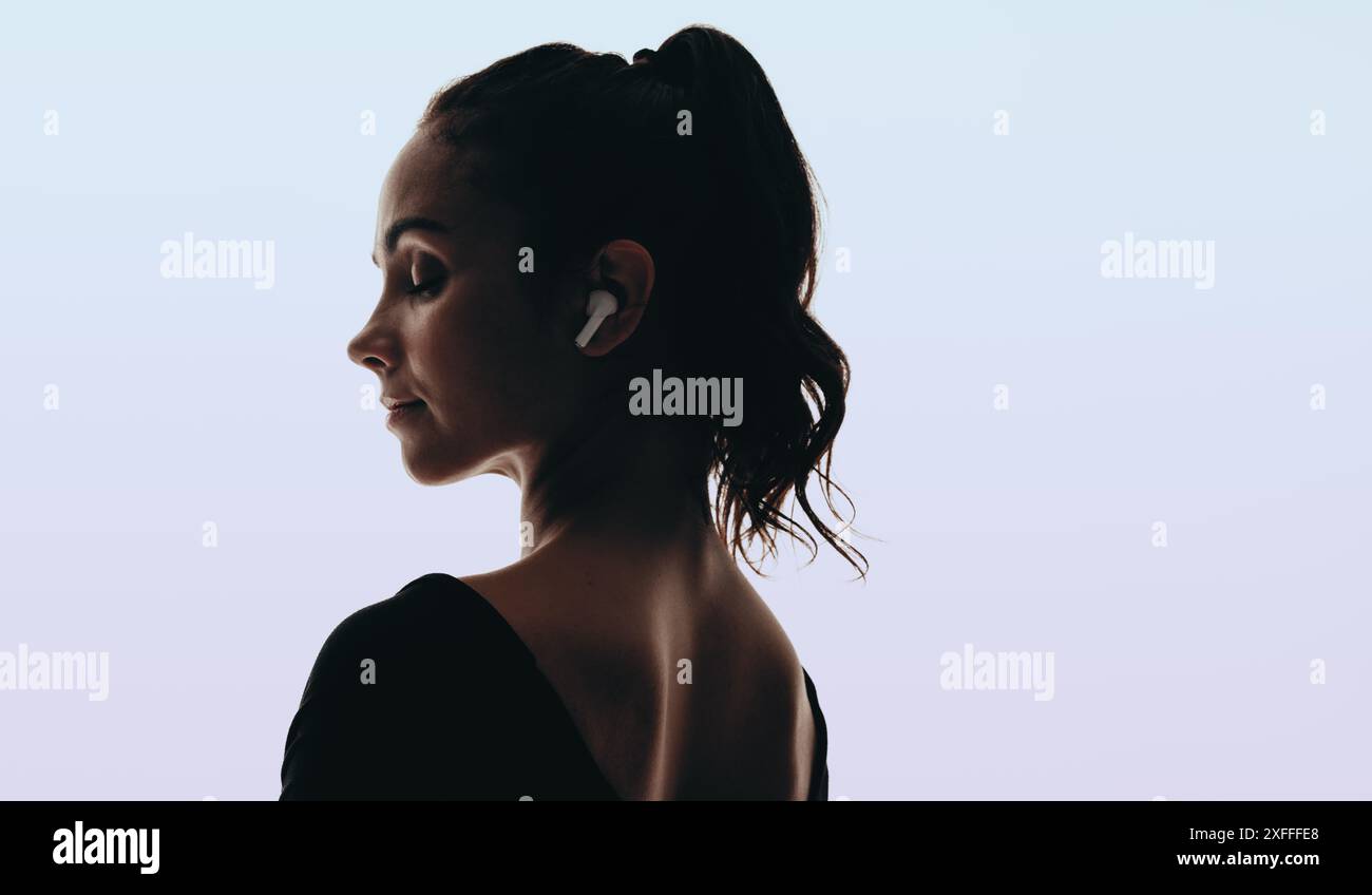 Woman with a ponytail stands in a studio, eyes closed in peaceful ...