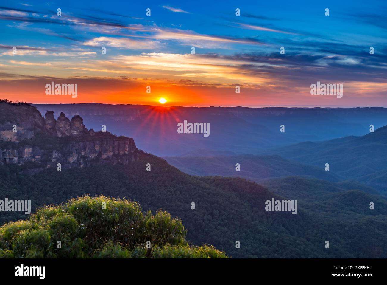 A vibrant sunset illuminates the iconic Three Sisters rock formation in ...