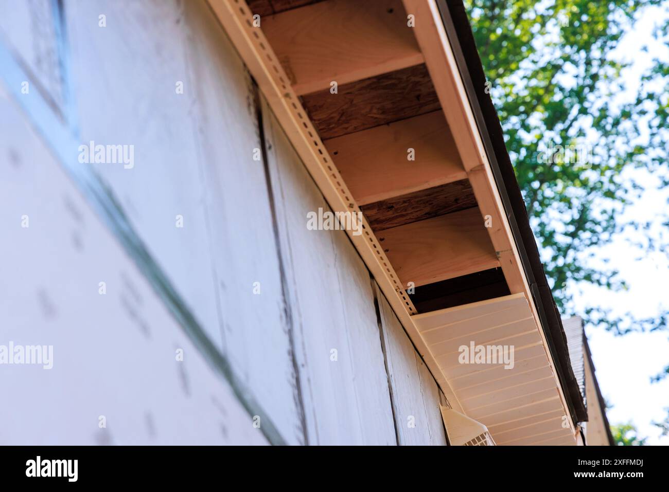 An employee installs soffit on roof corner of house constructed from ...