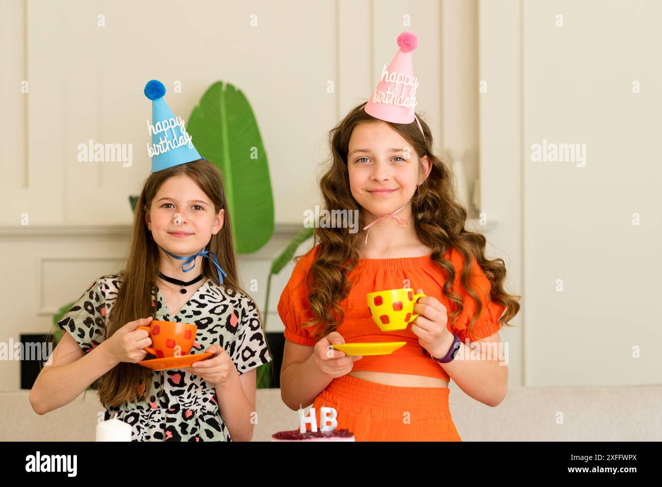 Two girls wearing birthday hats and holding colorful cups, celebrating ...