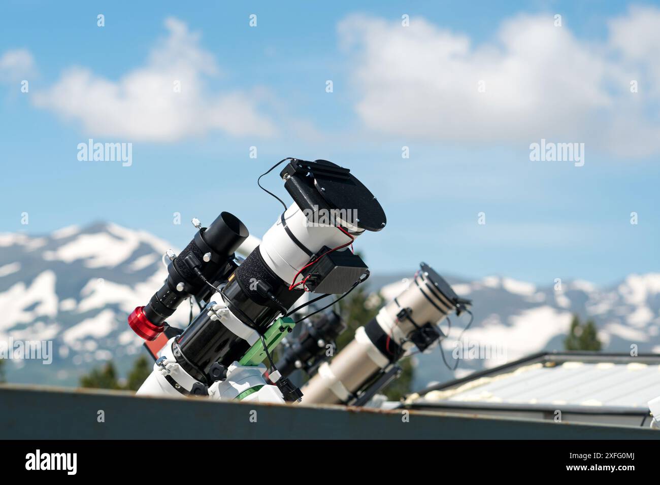 Telescopes on observatory rooftop with mountains and blue sky. Device ...