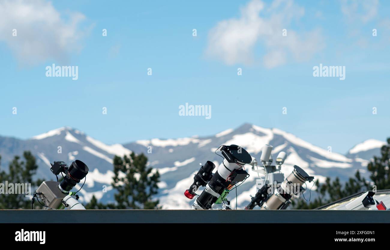 Telescopes on rooftop with snow-covered mountains in background. Device ...