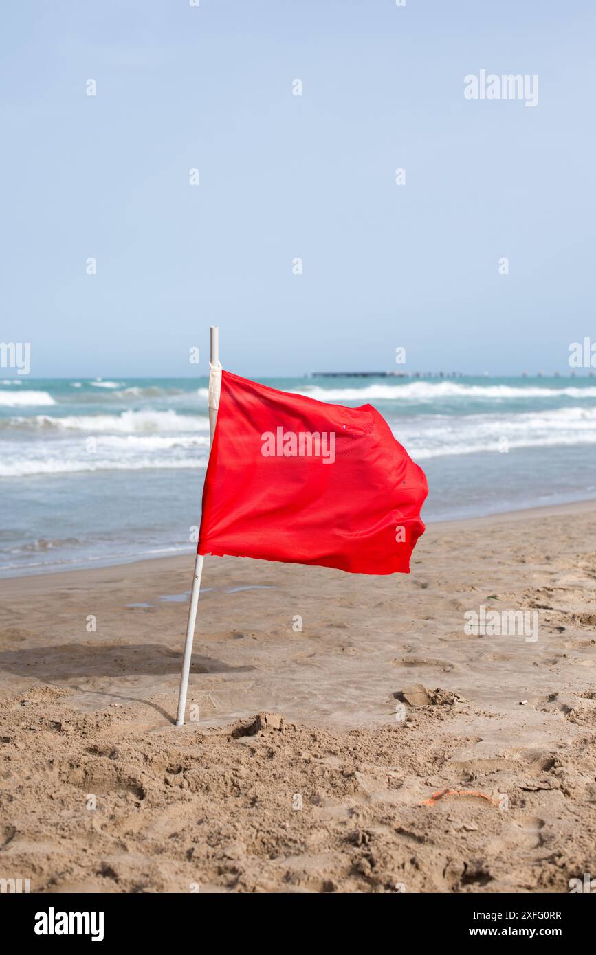 red flag waving in the wind on a sandy beach, warning of dangerous ...