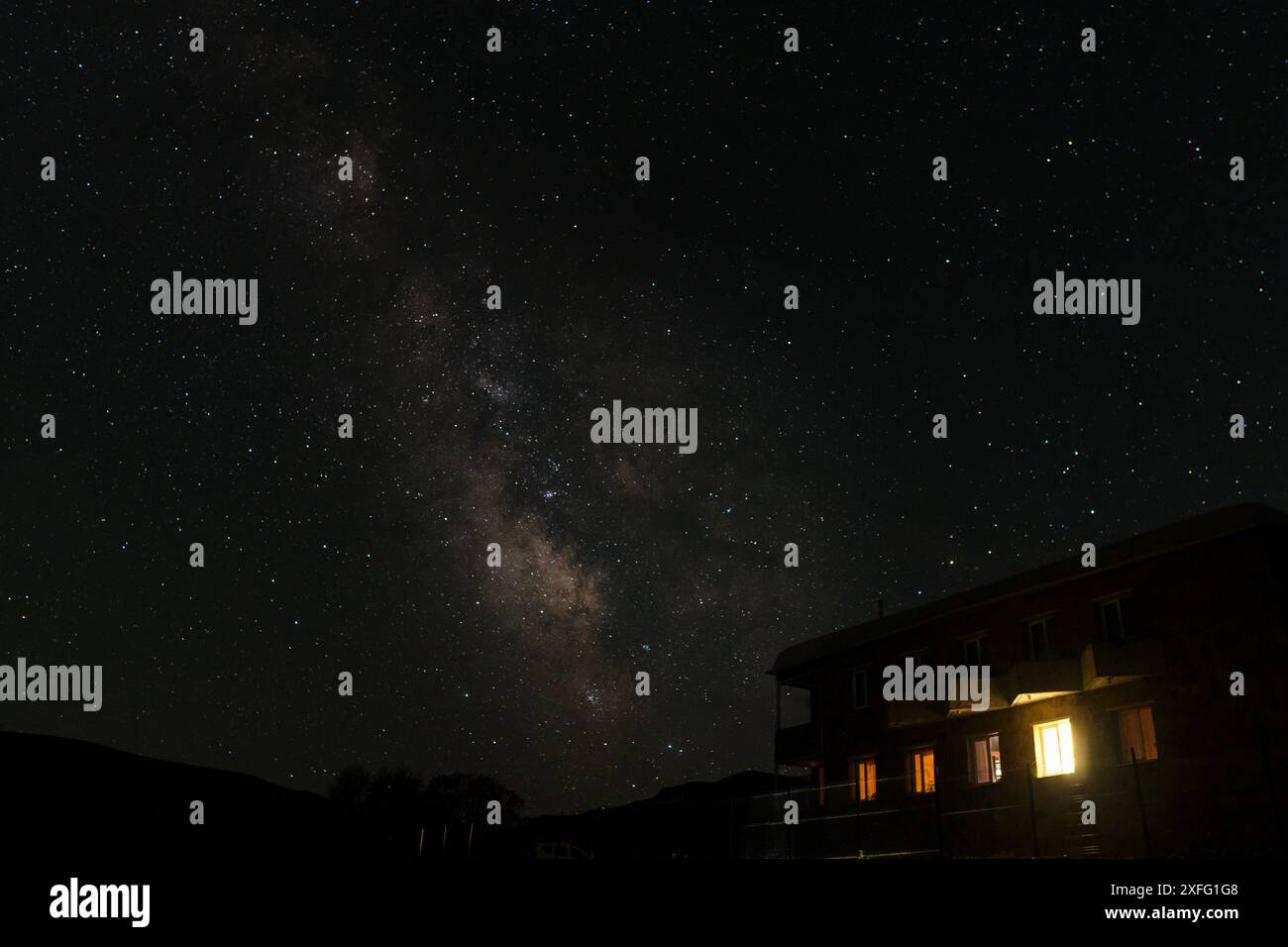 Starry night sky with the Milky Way and a building lit from within ...
