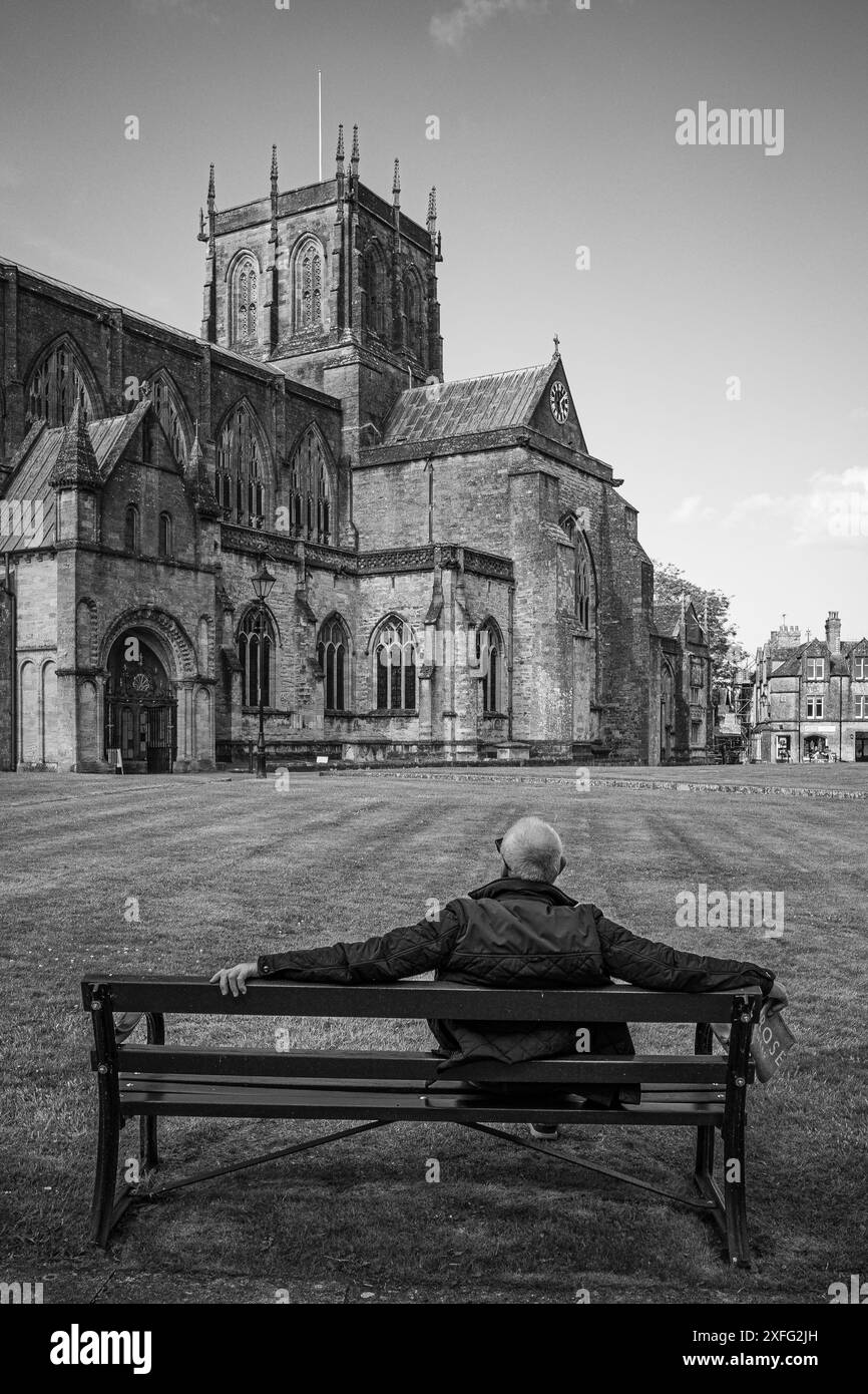 Lone man sitting looking at Sherborne Abbey, Sherborne, Dorset, England ...