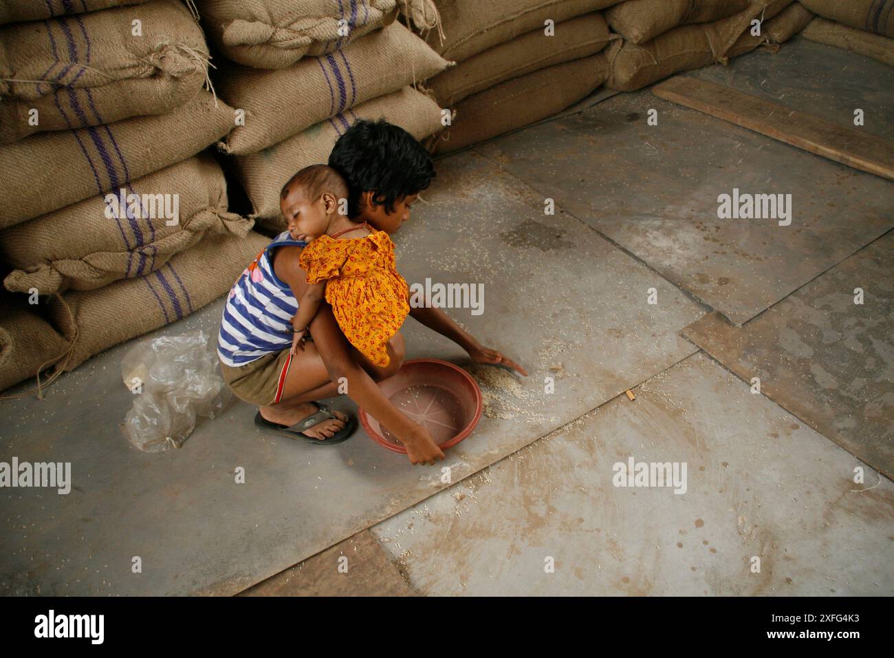 Tania, with her seven month-old brother Sajib, collects leftover rice ...