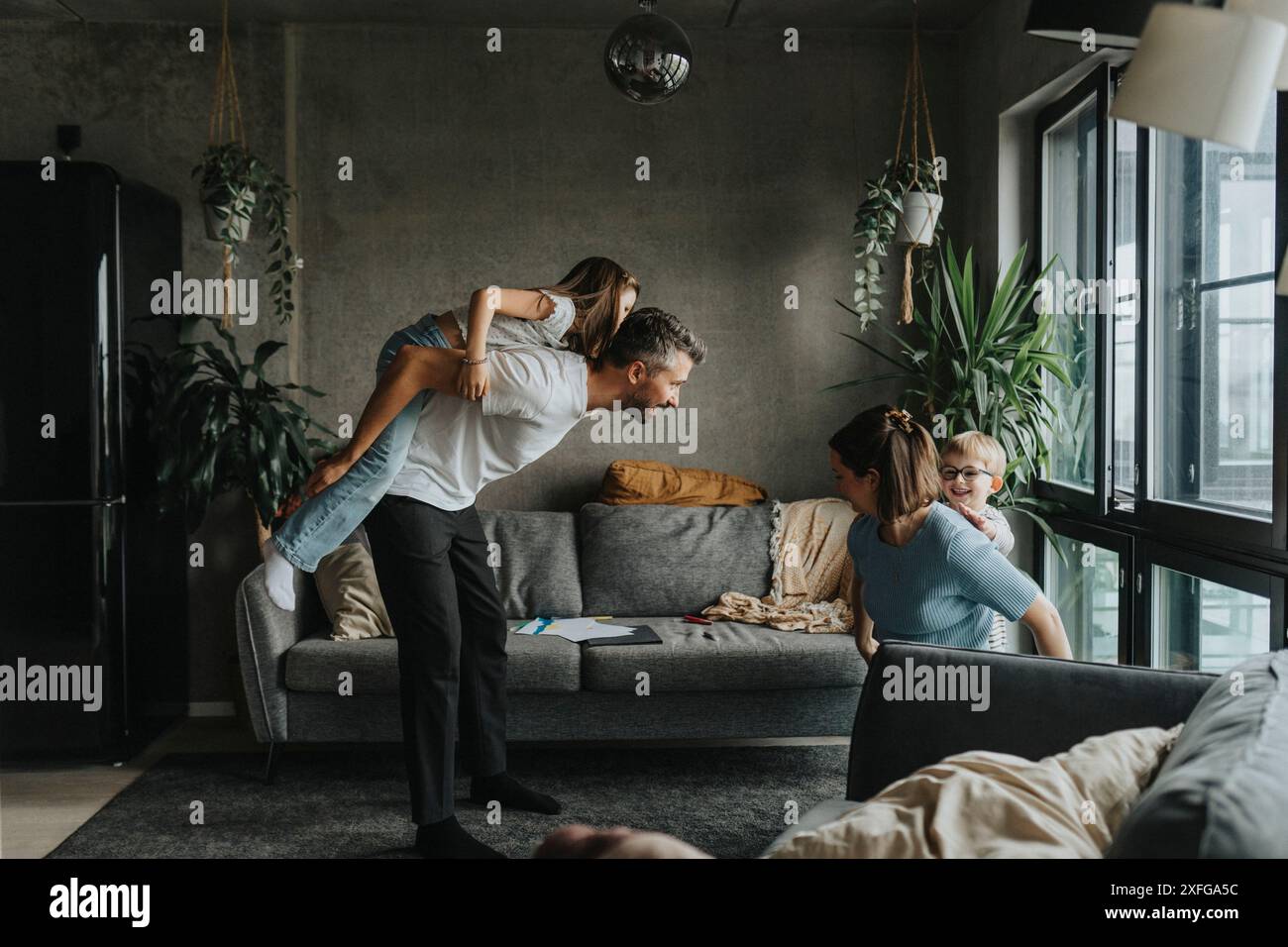 Father piggybacking daughter while spending leisure time with family in living room at home ...