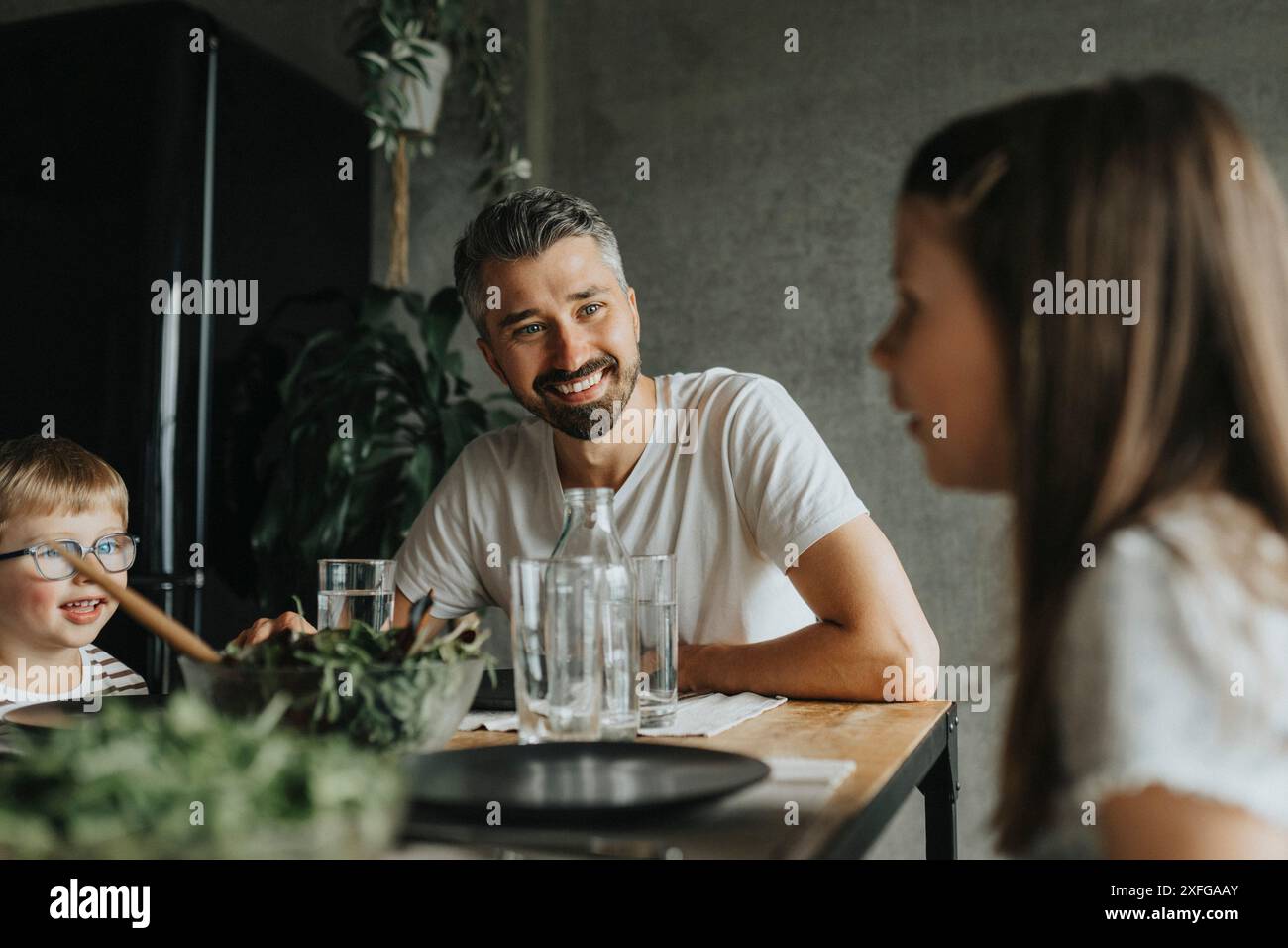 Happy father sitting near dining table with son and daughter at home ...