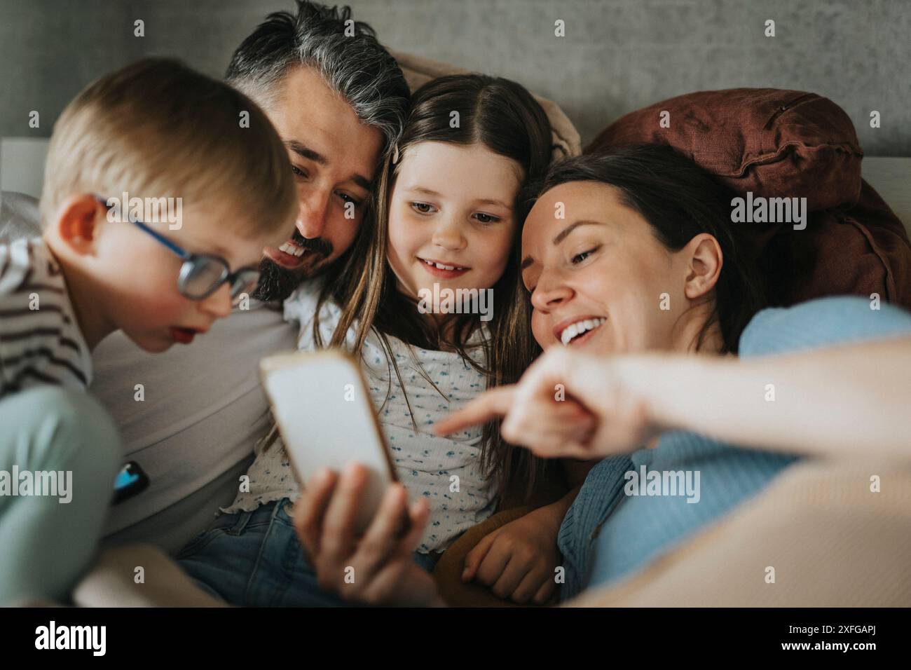 Happy family using smart phone while lying down on bed at home Stock ...