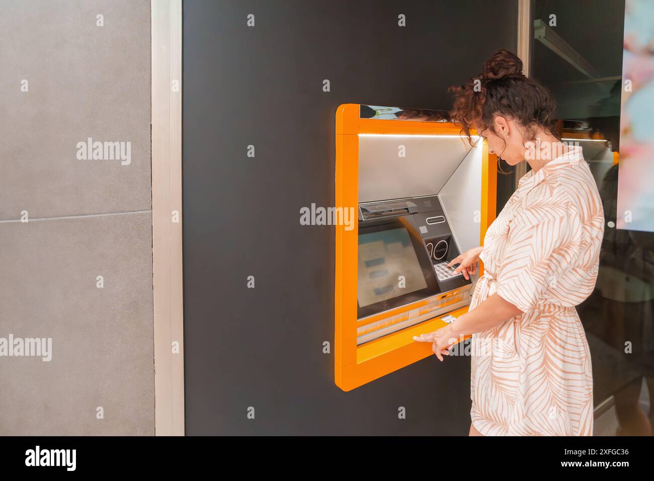 Hispanic Latin woman using ATM during daytime. Rear view Stock Photo ...