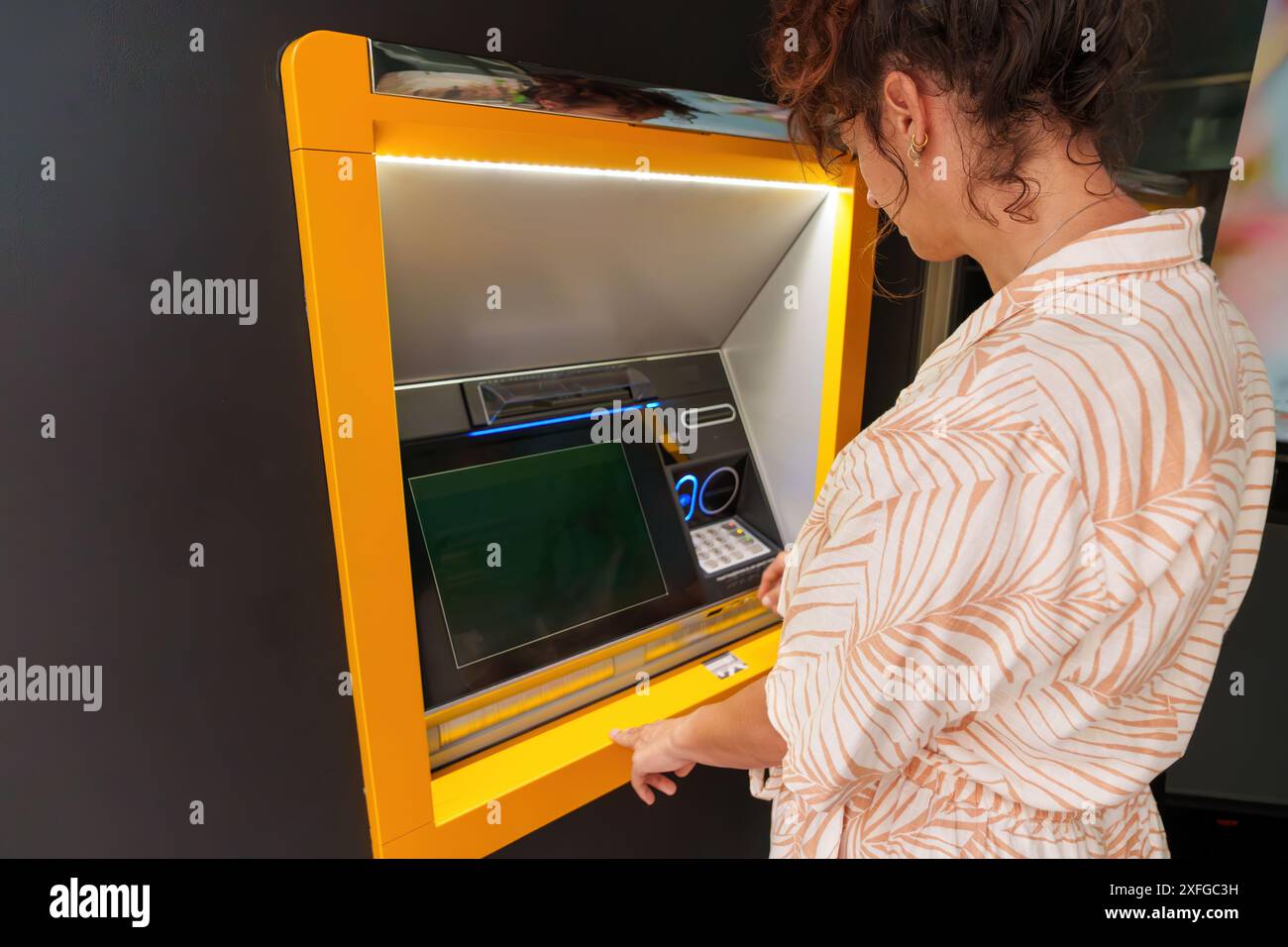Hispanic Latin woman using ATM during daytime. Rear view Stock Photo ...