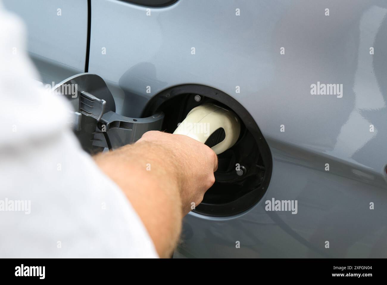 Man inserting plug into electric car socket at charging station ...