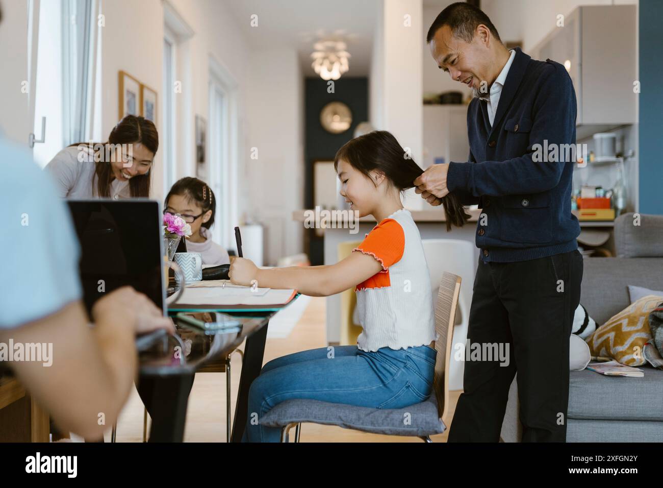 Father tying hair of daughter sitting on chair and doing homework Stock ...