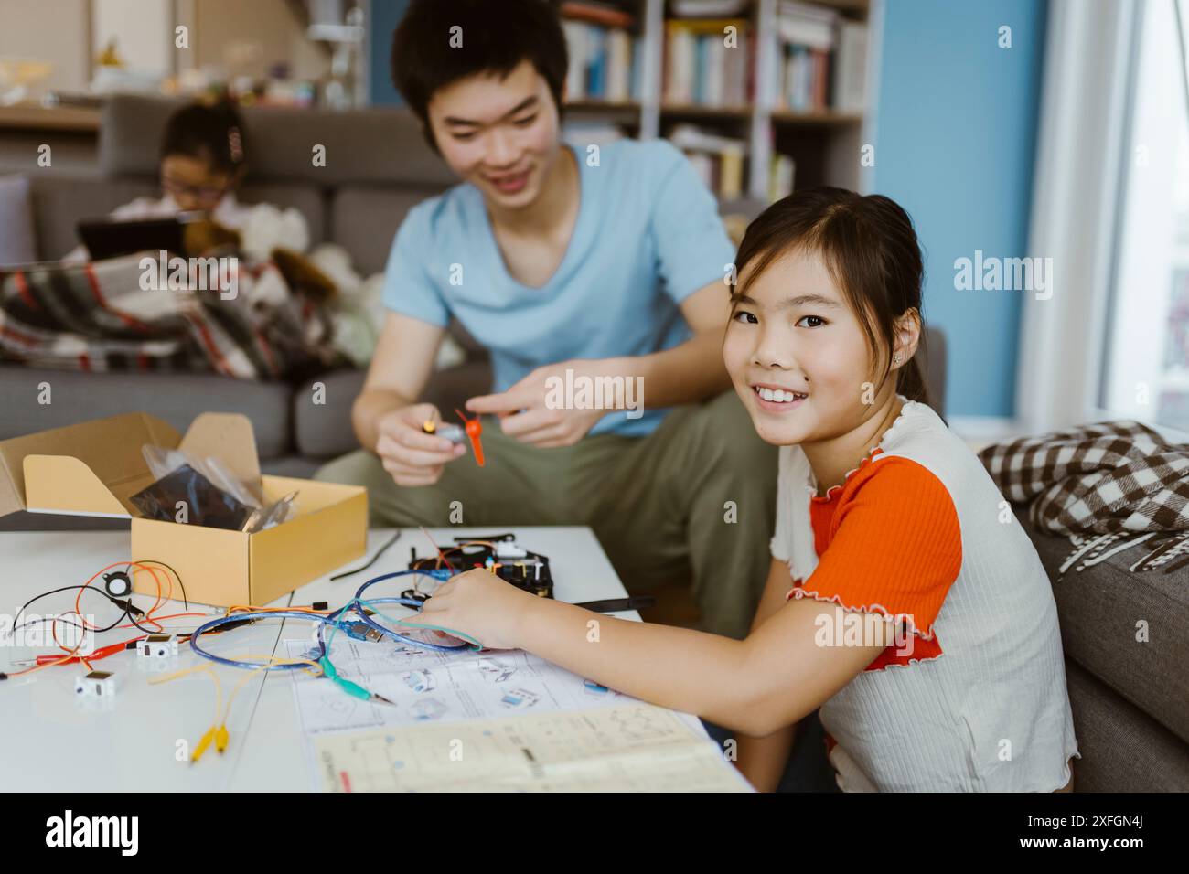 Smiling portrait of girl making science project sitting with brother at ...