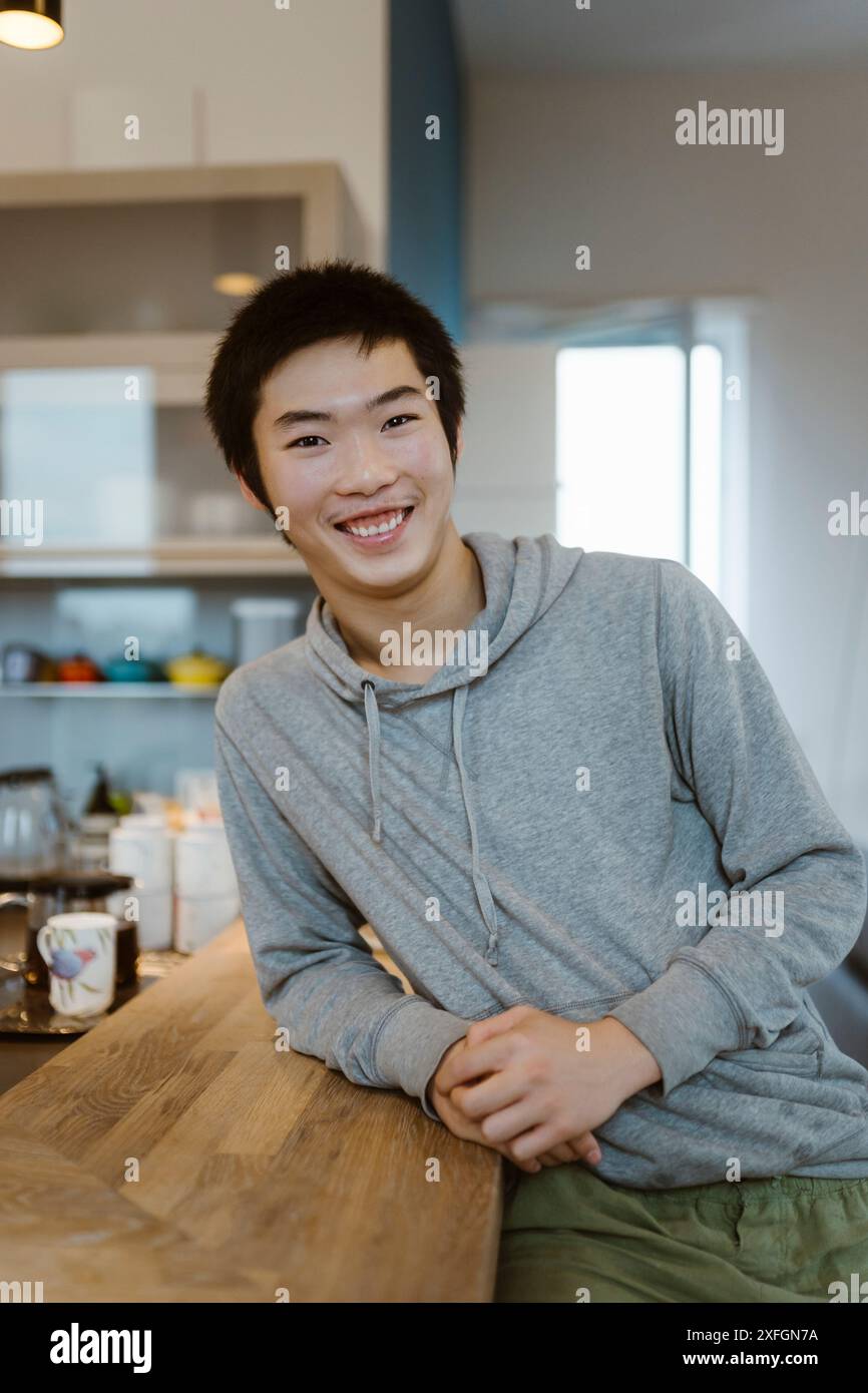 Portrait of smiling teenage boy leaning on wooden counter at home Stock ...