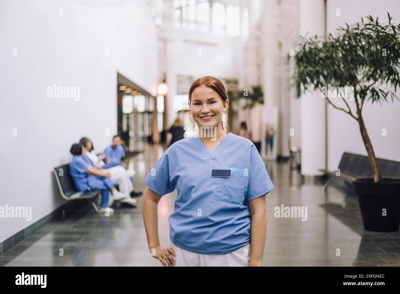 Portrait of smiling female medical trainee standing with hand on hip in ...