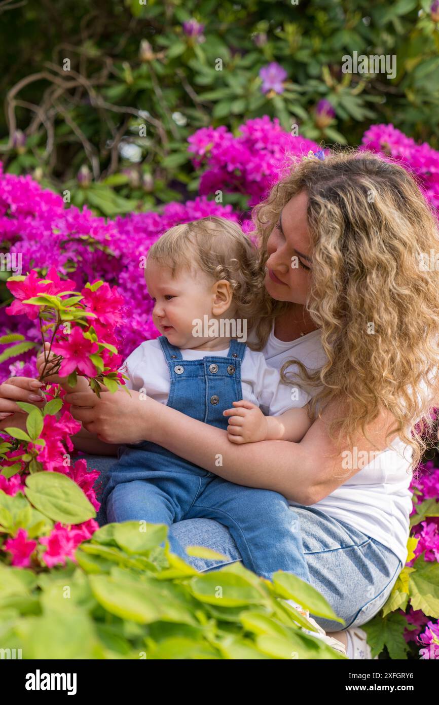 A happy mother with wavy hair holds and hugs a little blond boy with ...