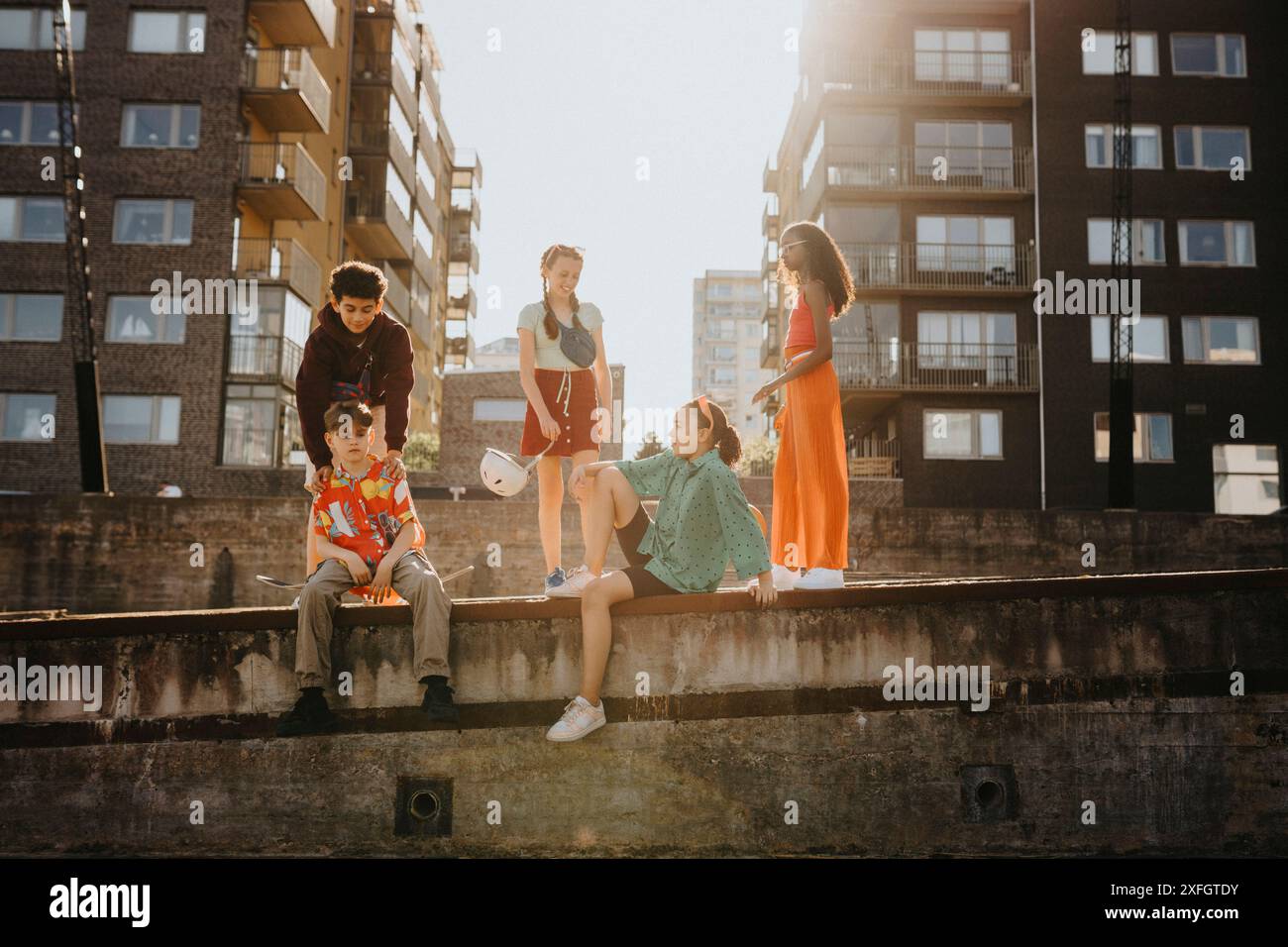 Group of friends sitting on wall against residential buildings Stock ...