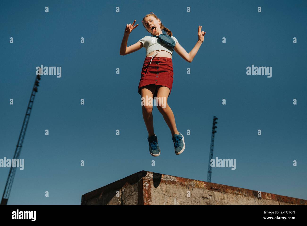 Carefree girl jumping in mid-air while doing peace sign against blue ...