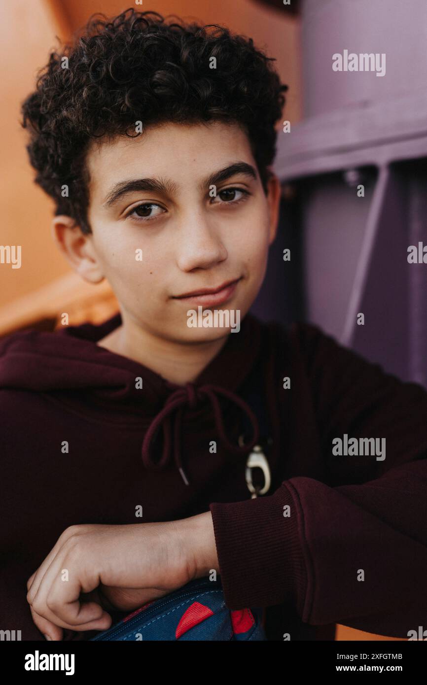 Portrait of boy wearing maroon hooded shirt with curly hair Stock Photo ...