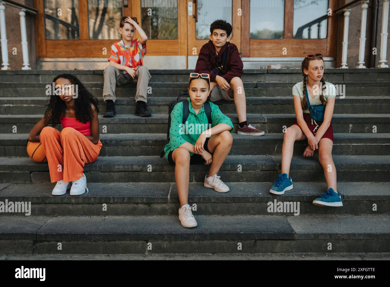 Portrait of girl sitting with friends on staircase in front of school ...