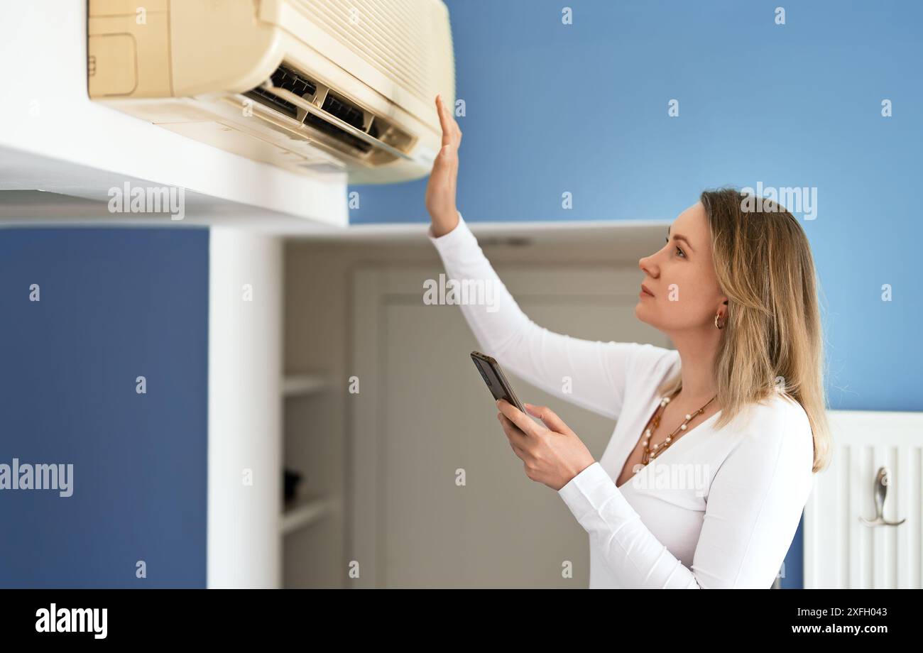 Woman controls a smart air conditioner using a remote control on her ...