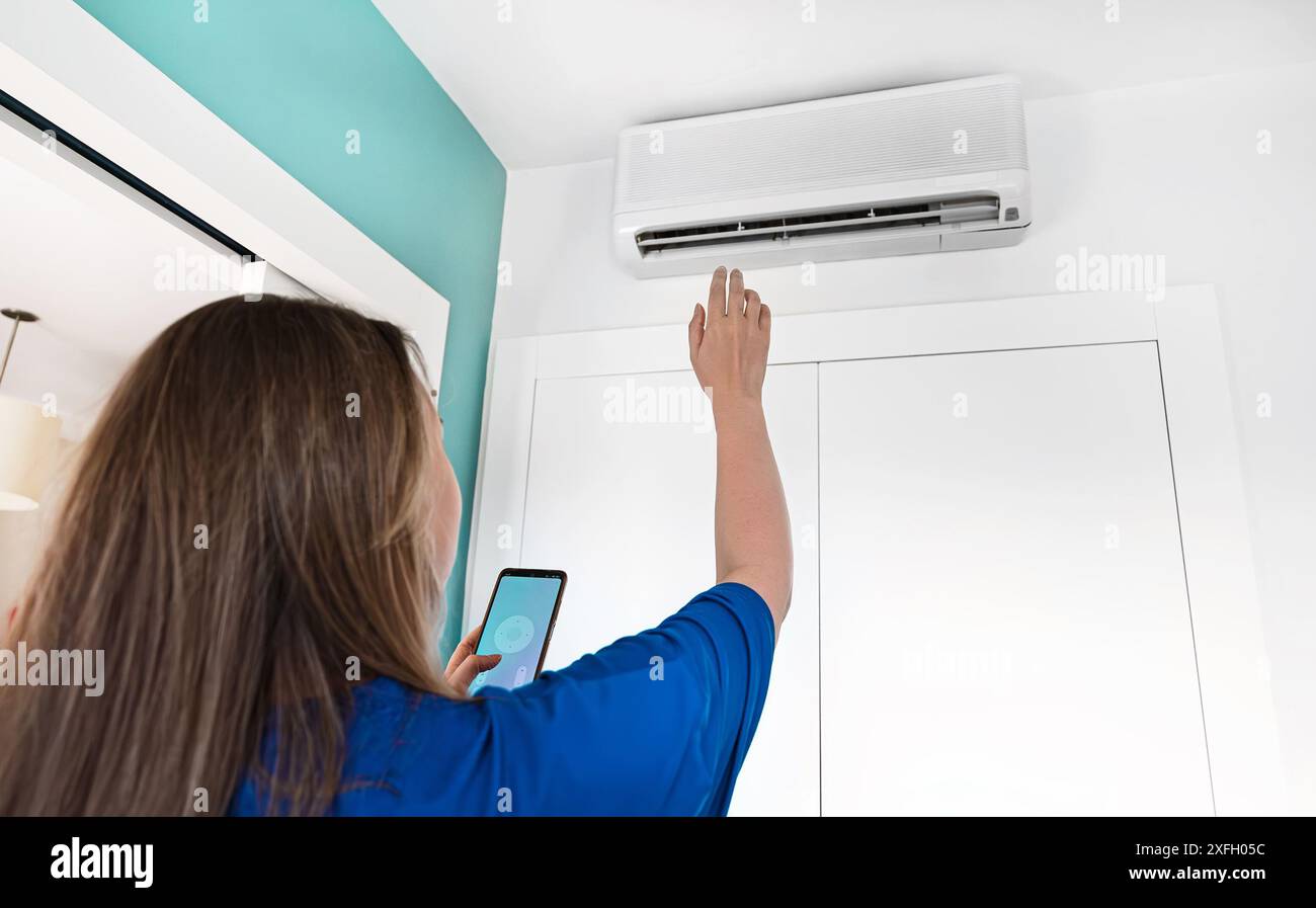 Woman controls a smart air conditioner using a remote control on her ...