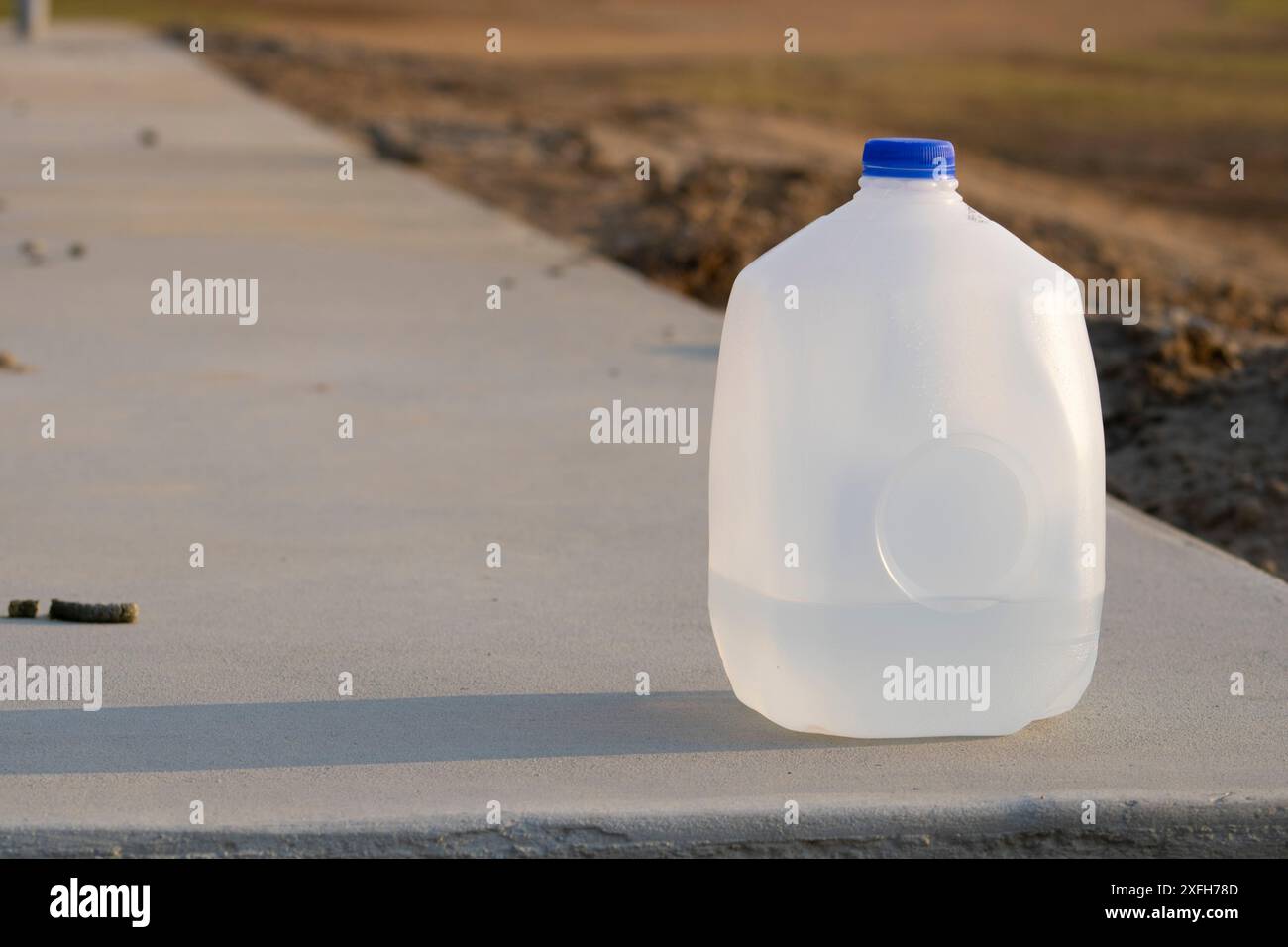 quarter full water gallon container with blue lid sitting on sidewalk ...