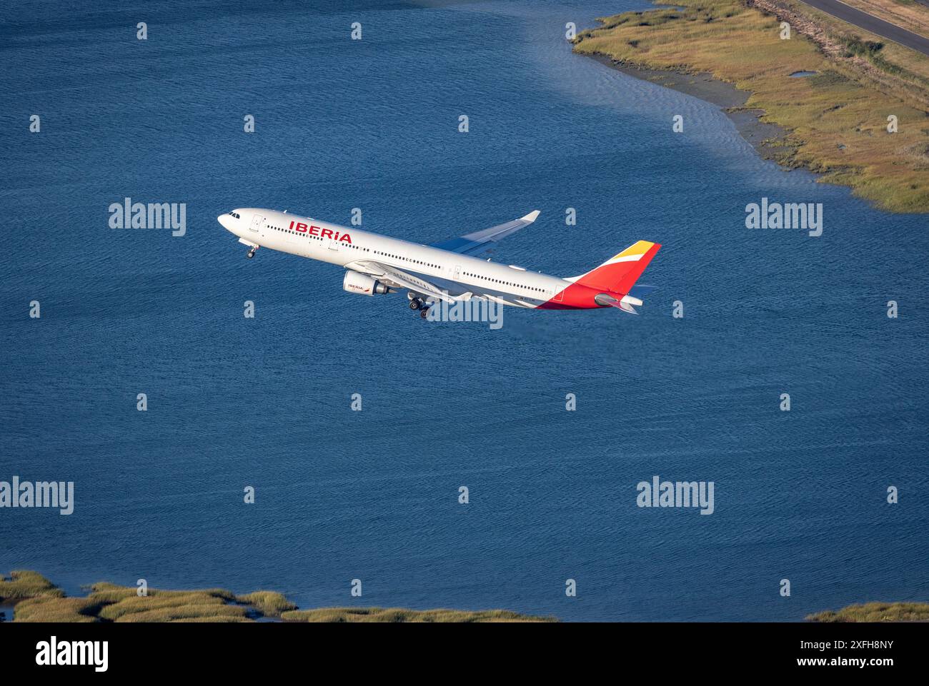Aerial view of an Iberia airplane taking off over a body of water with ...