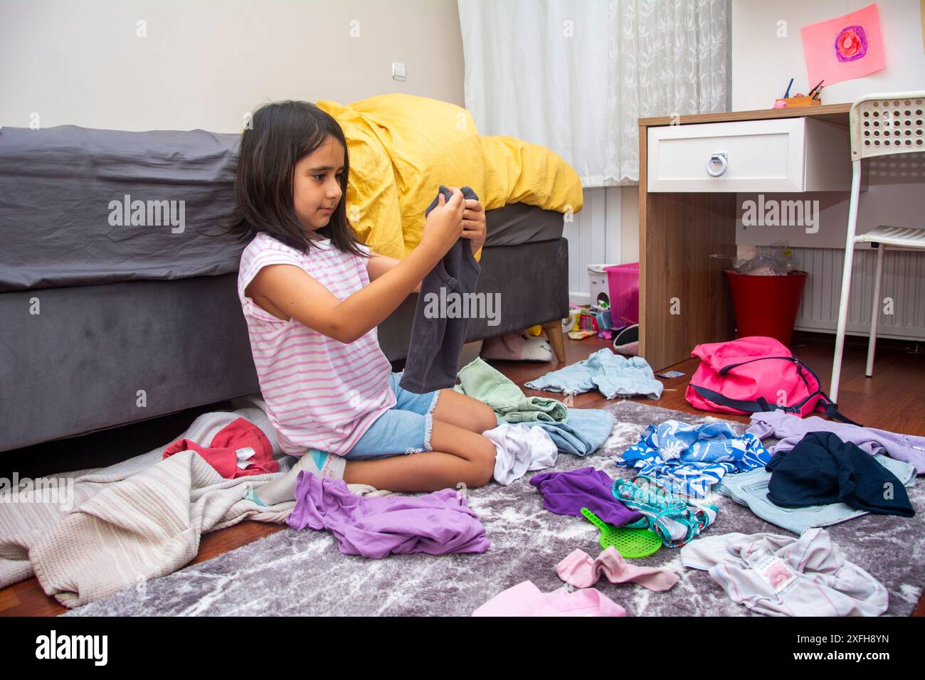 Little girl folding clothes in her messy room Stock Photo - Alamy