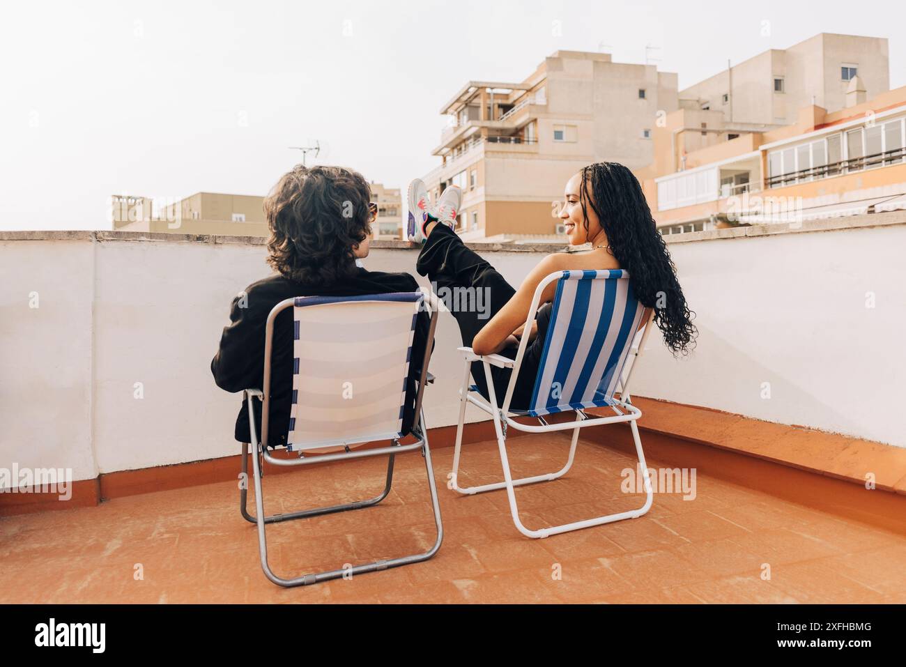 Male and female friends sitting on chairs on building rooftop Stock ...