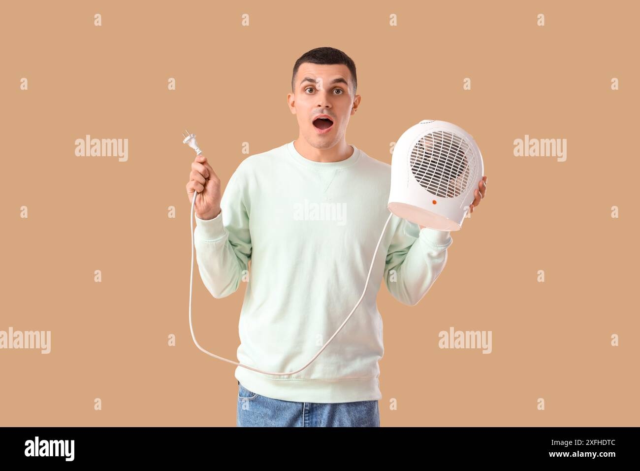 Shocked young man with electric fan heater on beige background Stock ...