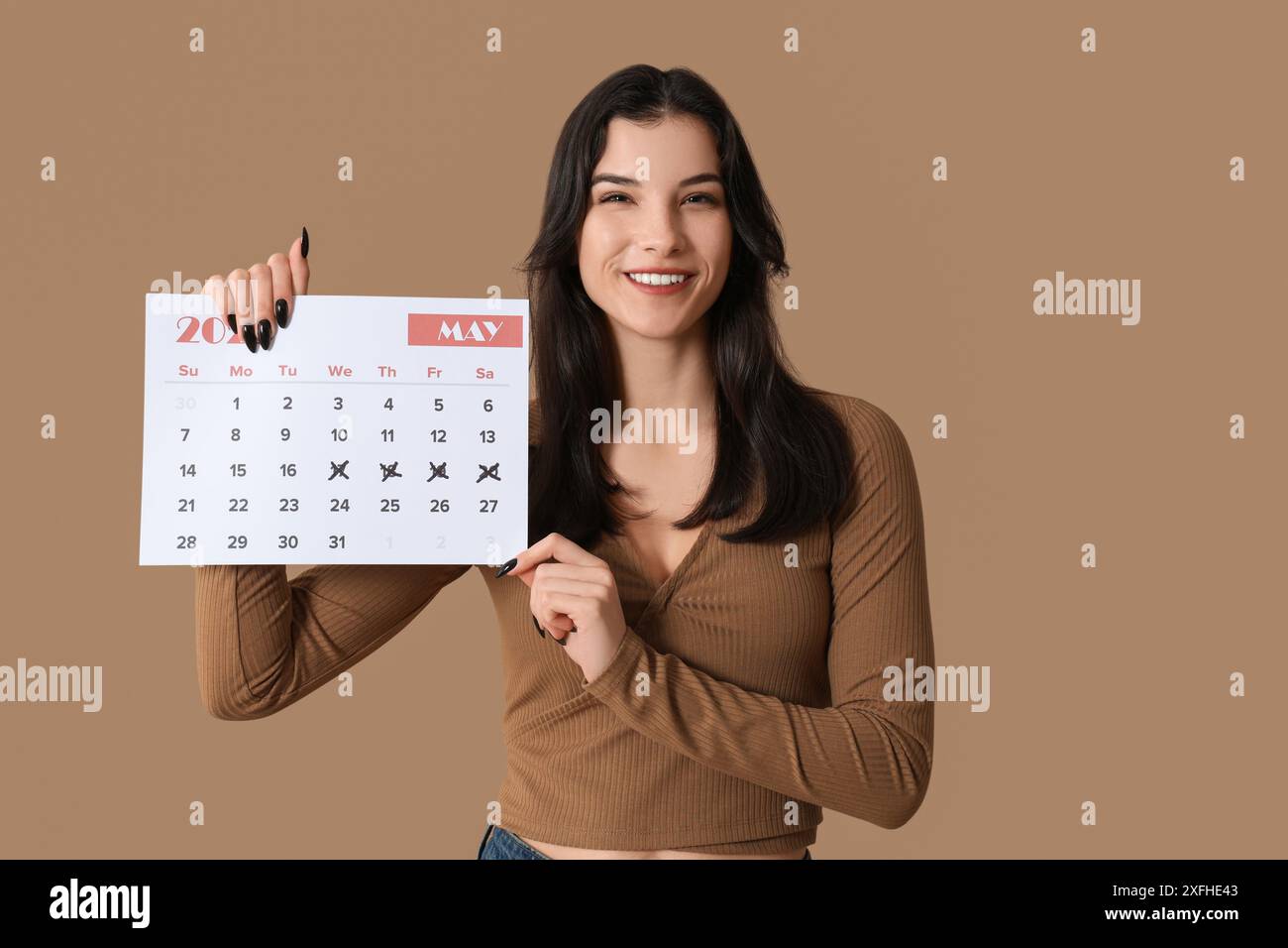 Pretty young woman holding calendar with marked days on brown ...