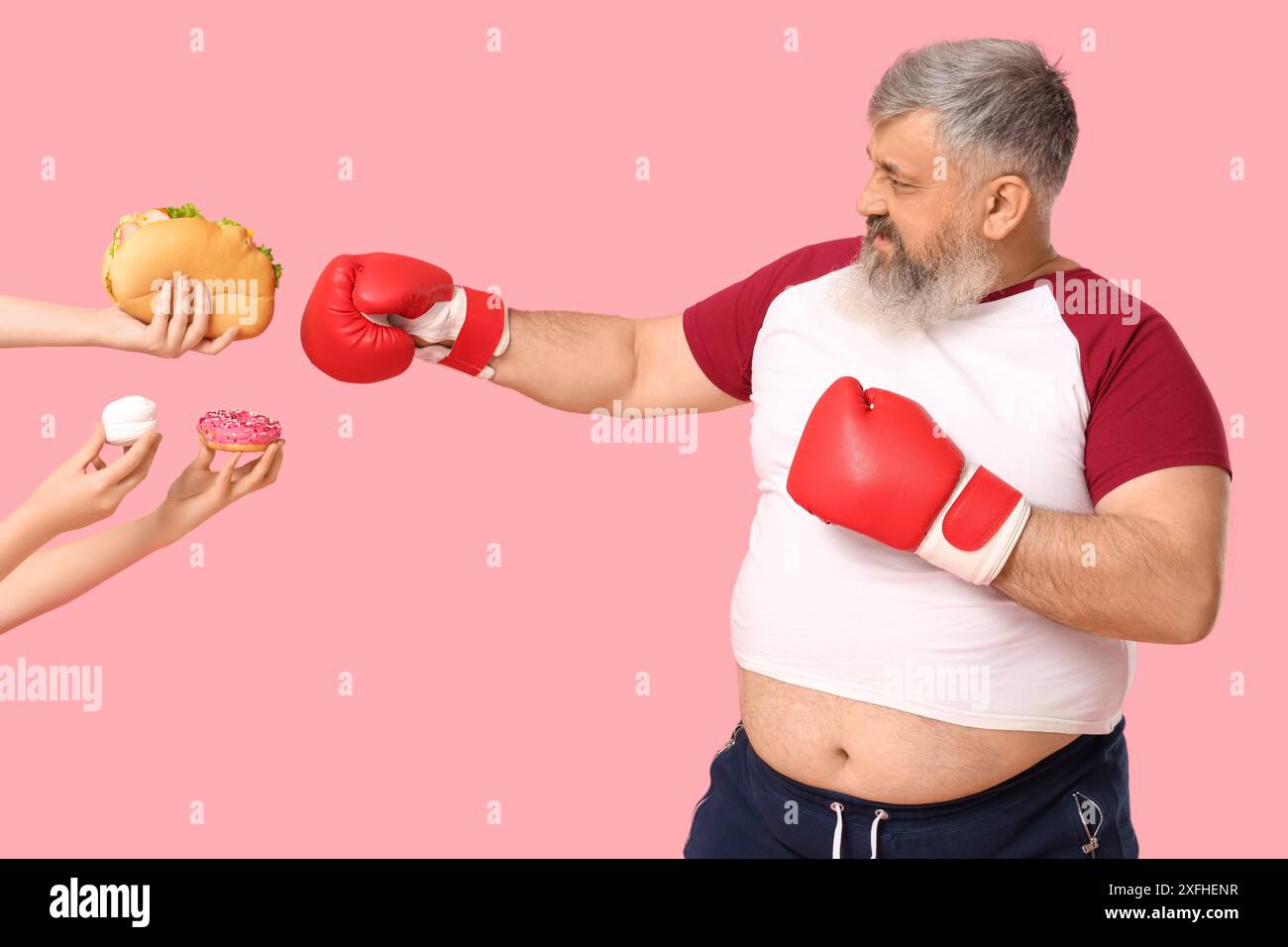 Overweight mature man in boxing gloves fighting unhealthy food on pink ...
