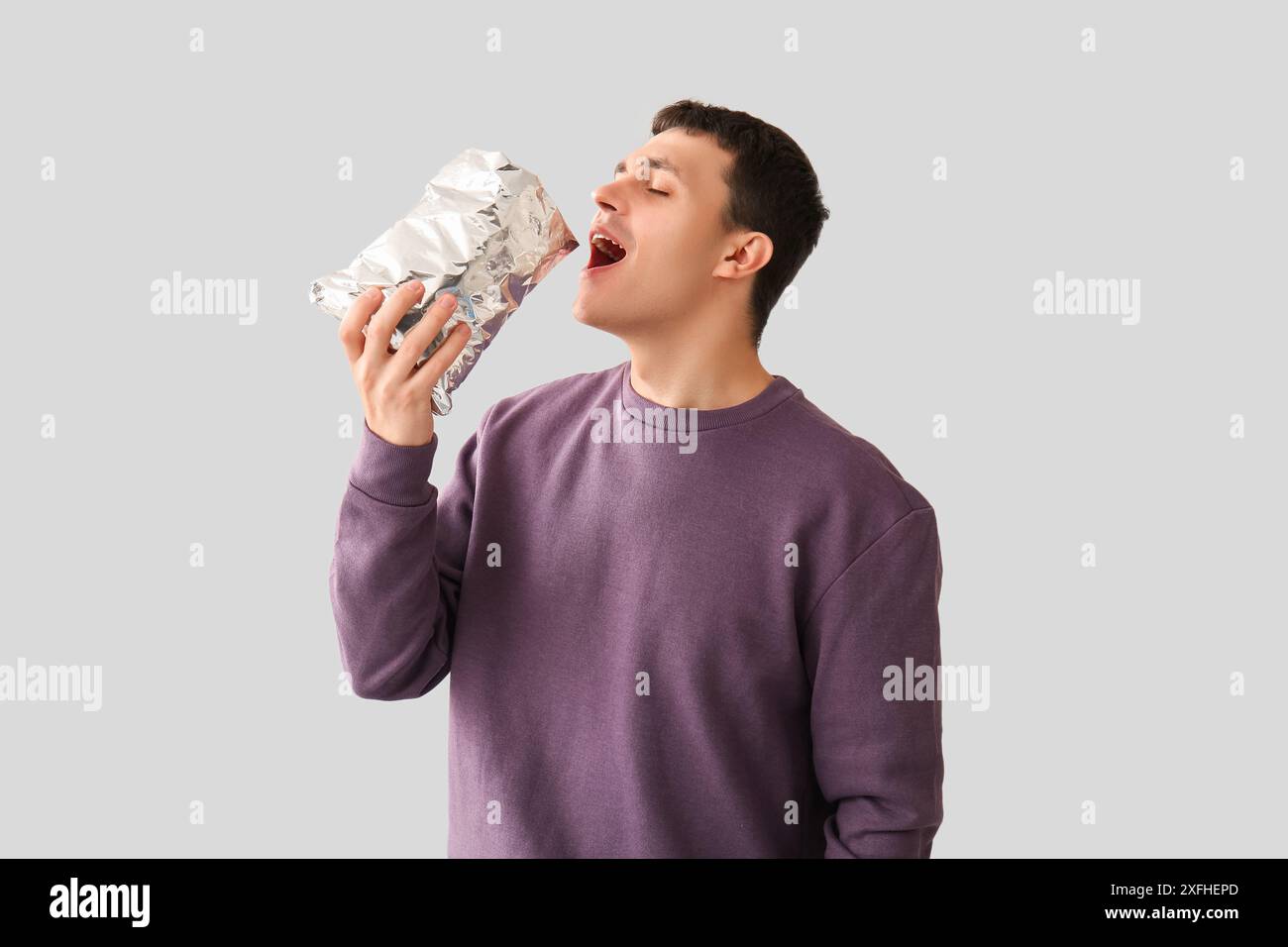 Young man eating potato chips on light background Stock Photo - Alamy