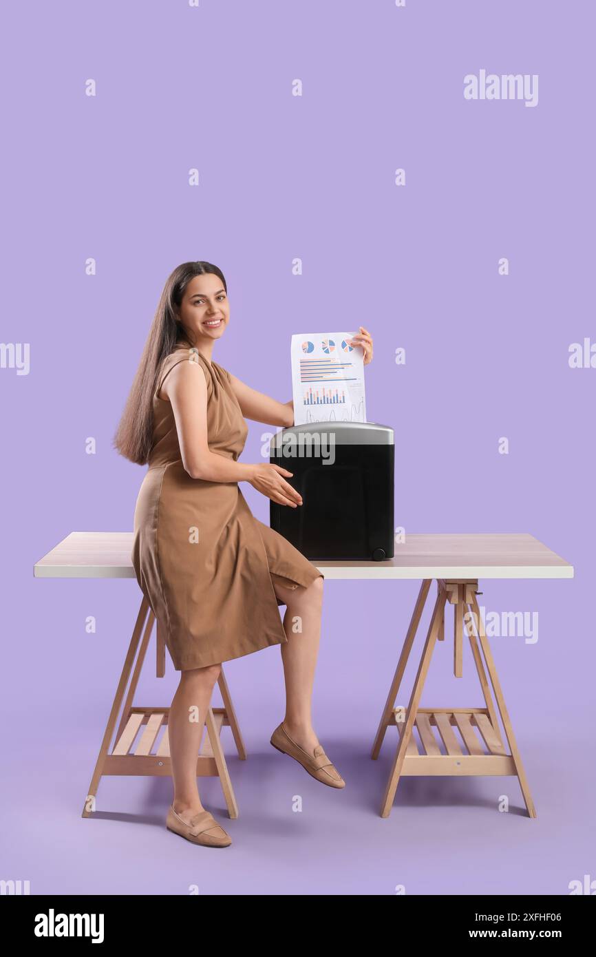 Happy young woman destroying documents using shredder on table against ...