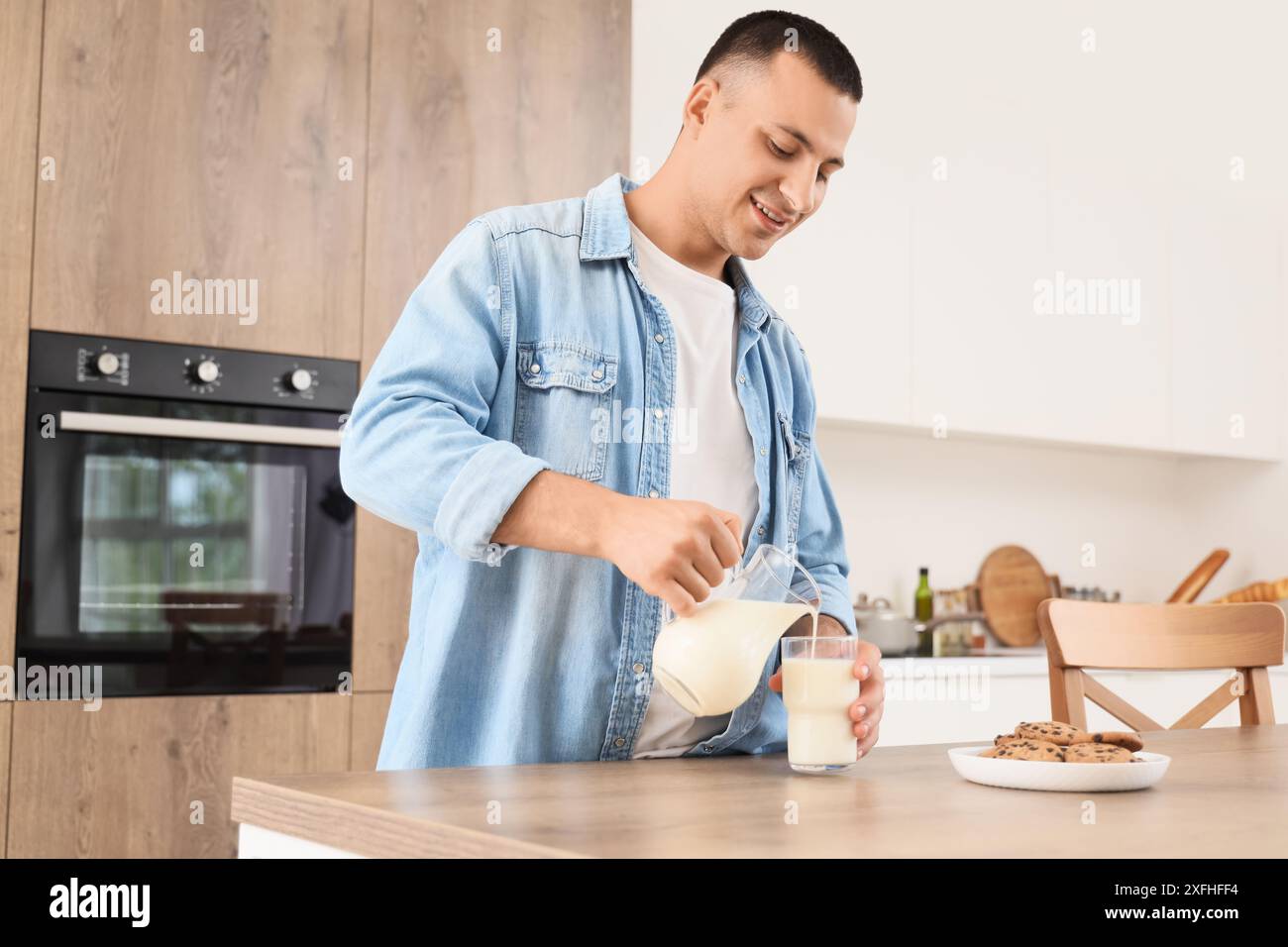Young man pouring milk from jug into glass in kitchen Stock Photo - Alamy