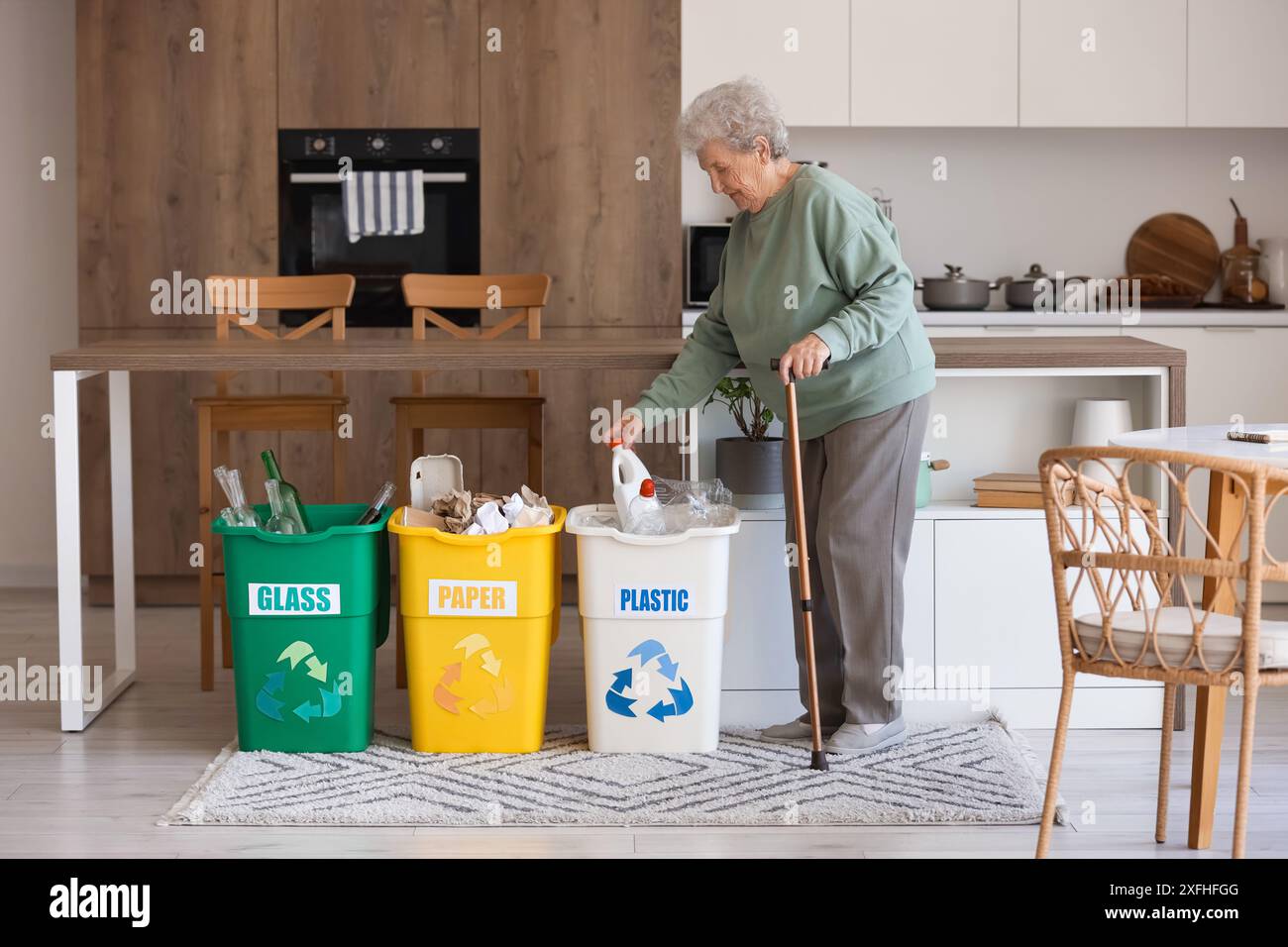 Senior woman throwing plastic bottle into garbage bin in kitchen. Waste ...