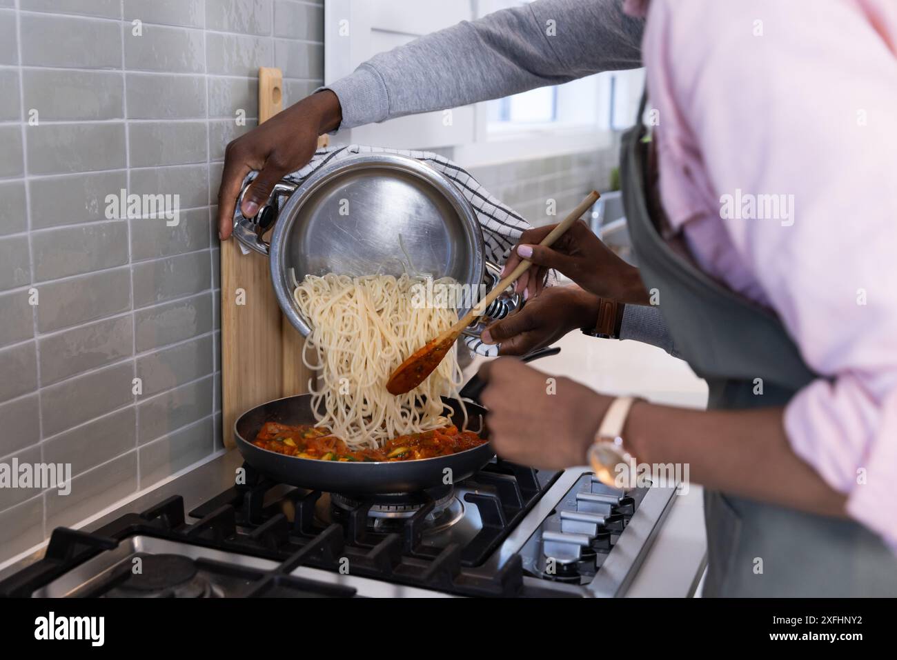 Cooking pasta together, couple pouring spaghetti into pan with tomato ...