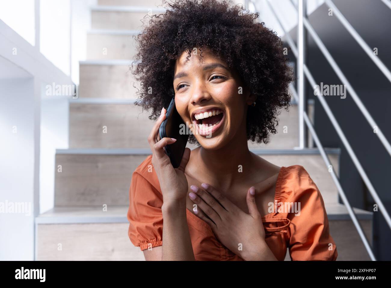 Talking on smartphone, woman sitting on stairs and laughing, enjoying conversation Stock Photo ...