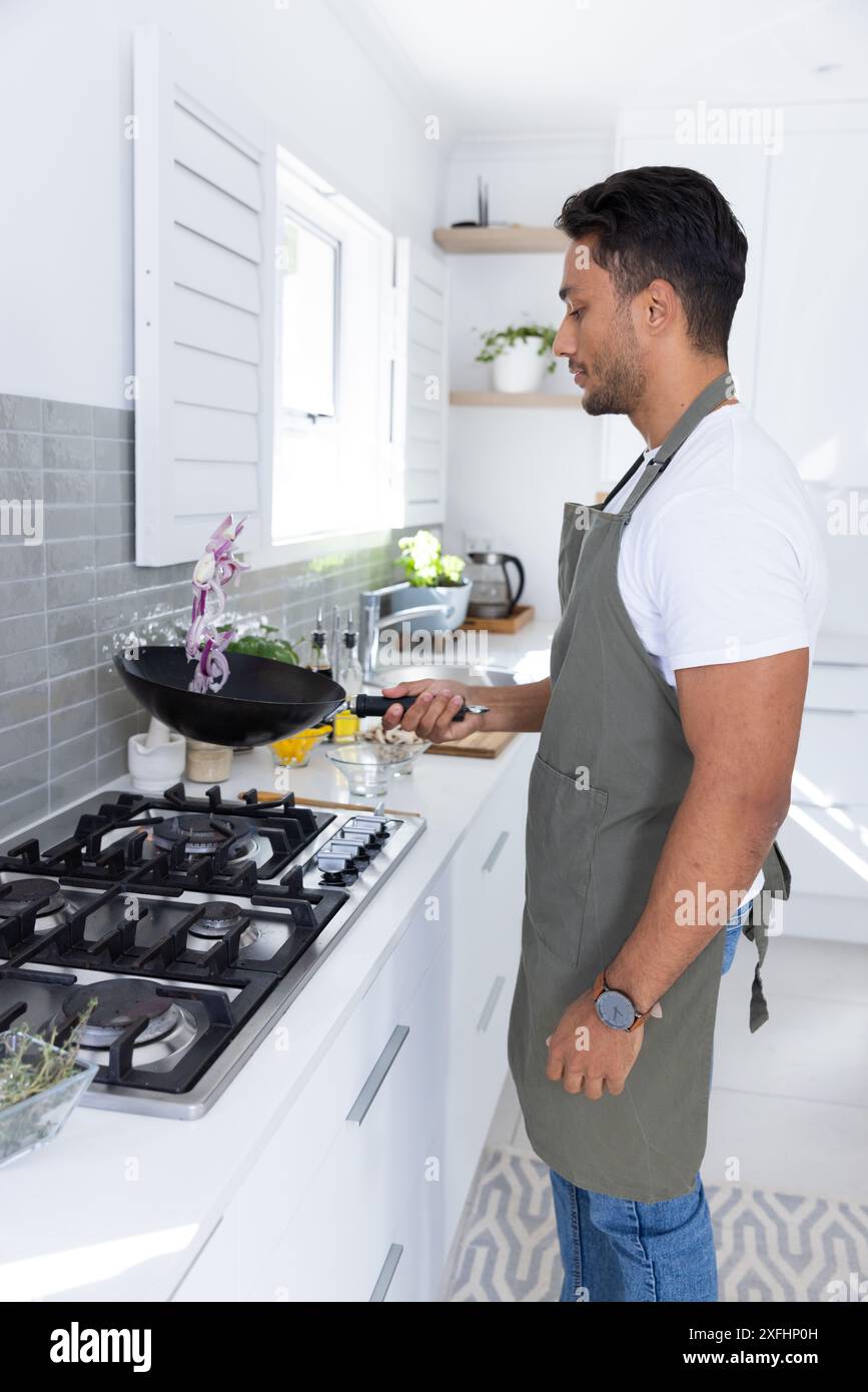 Cooking in kitchen, man flipping vegetables in frying pan, wearing ...