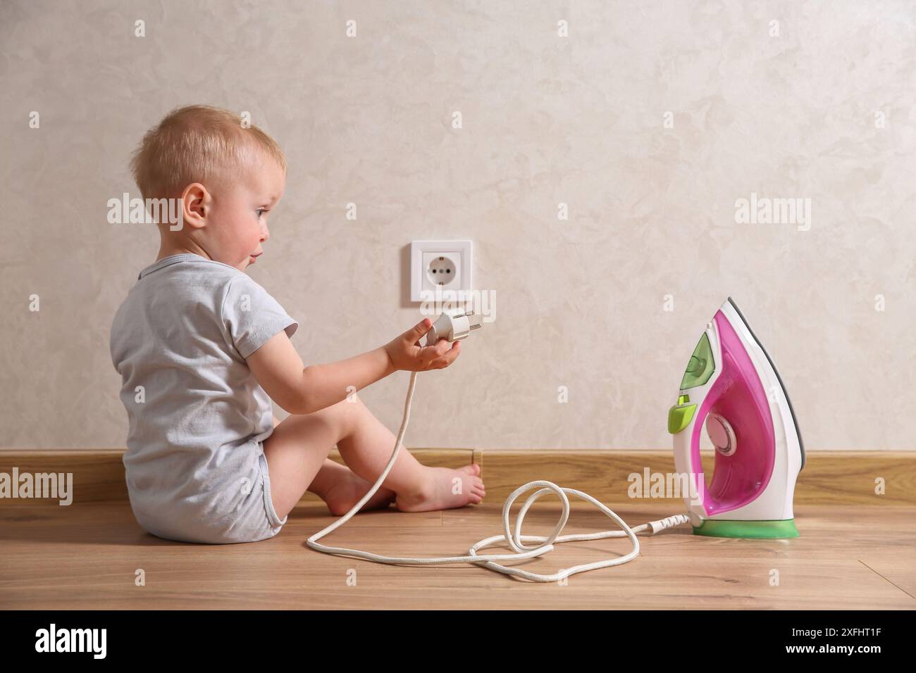 Little child playing with electrical socket and iron plug indoors ...