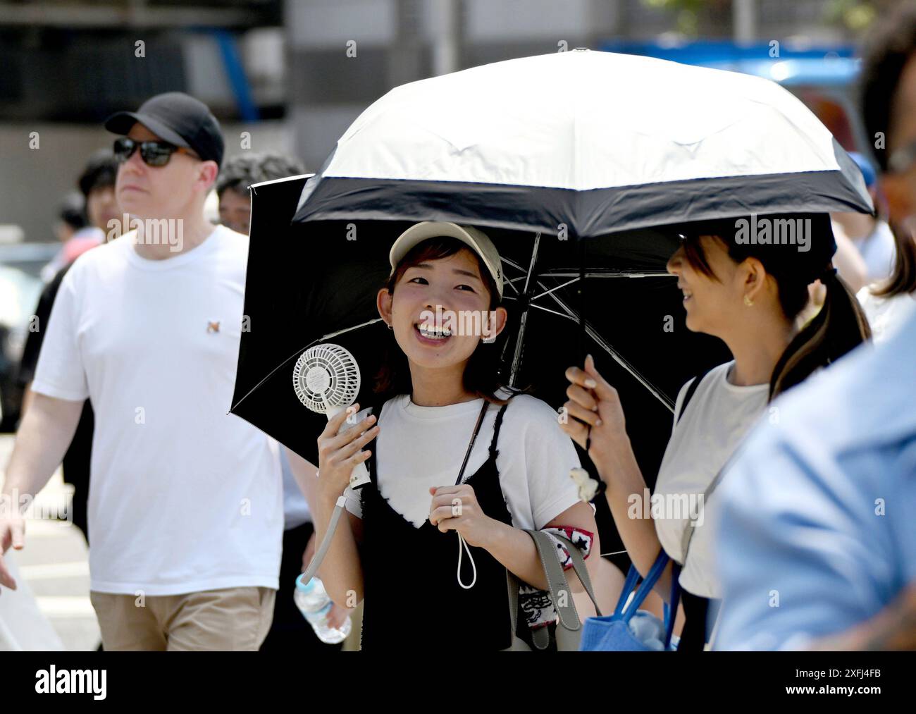 Pedestrians walk past Shibuya Scramble Crossing using a portable fan ...