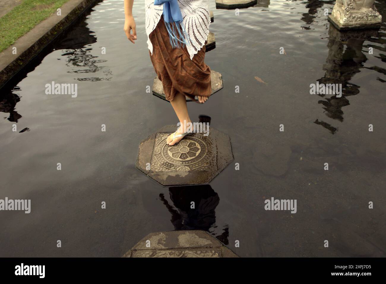 A woman walking on stone footsteps at Tirta Gangga water palace in ...