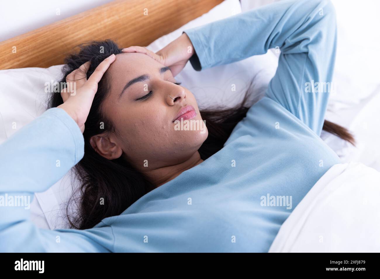 Relaxing in bed, woman with closed eyes massaging her temples. Relaxation, wellness, self-care ...