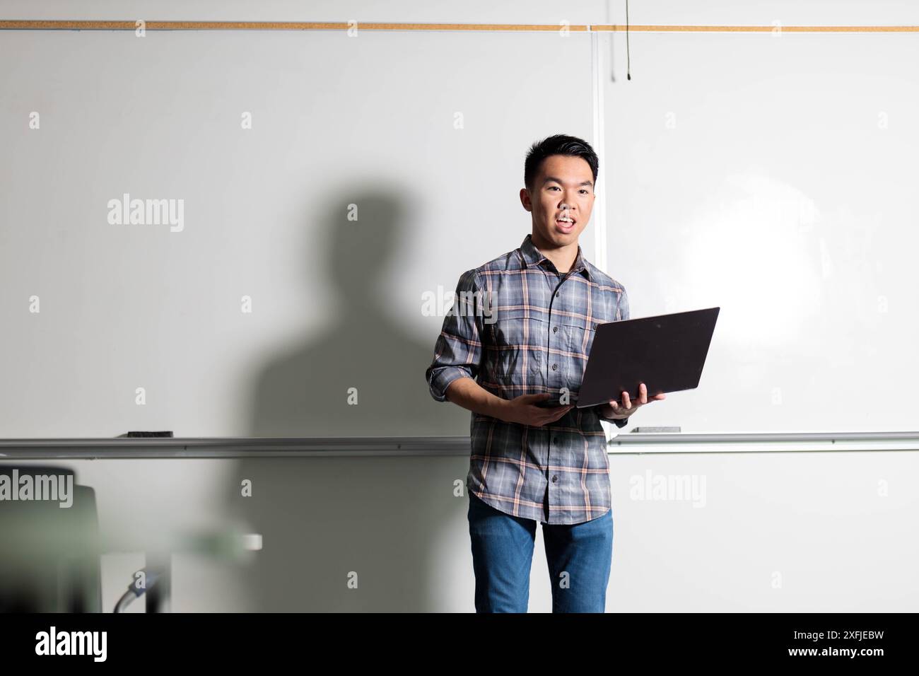 In a classroom, a male teenage student is giving a presentation speech ...