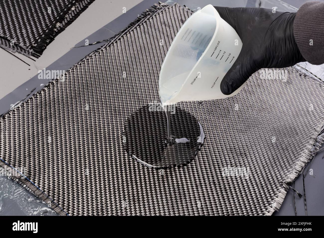 hand pouring epoxy resin on woven carbon fiber reinforcement cloth. Production manufacturing of ...