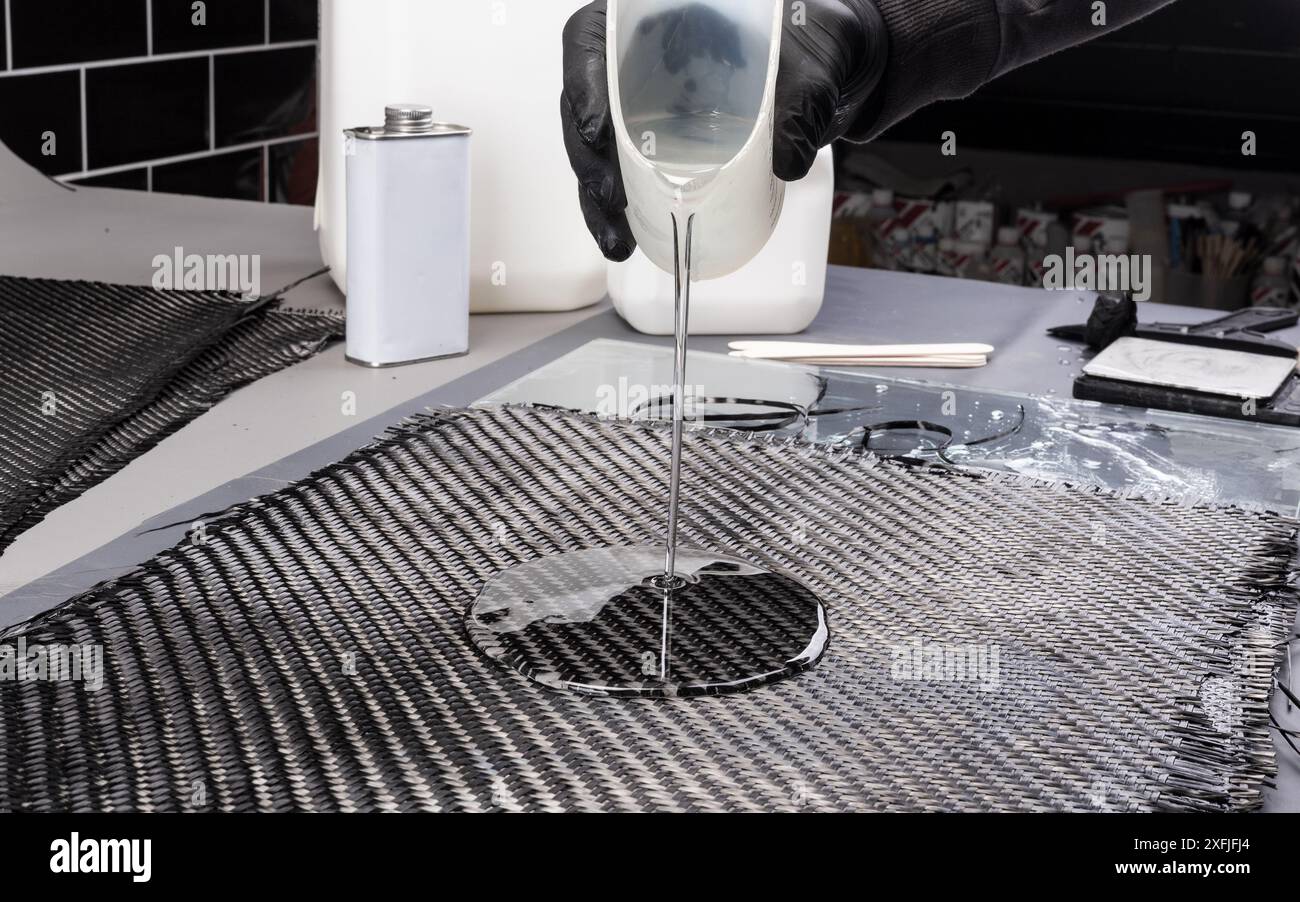 hand pouring epoxy resin on woven carbon fiber reinforcement cloth. Production manufacturing of ...