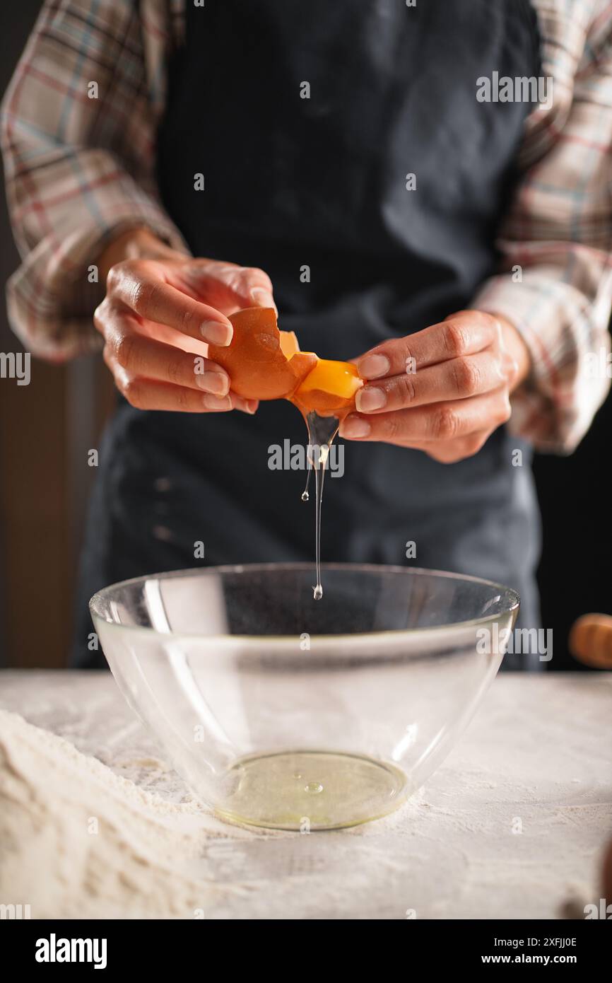 Close-up of female hands separating an egg yolk from the white over a clear bowl in the kitchen ...